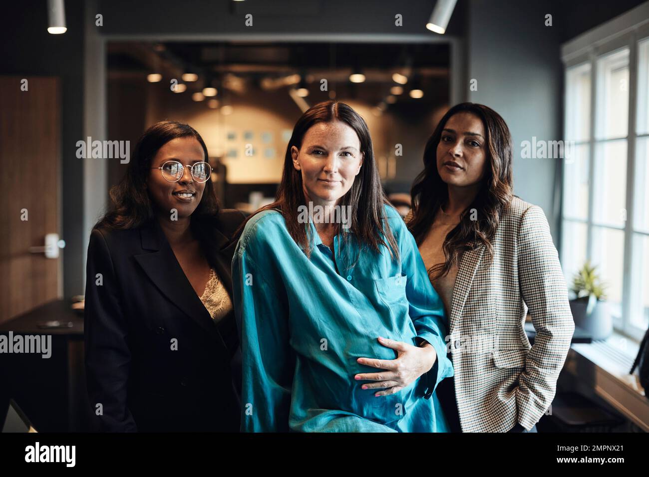Confident businesswomen with pregnant female colleague at office Stock ...