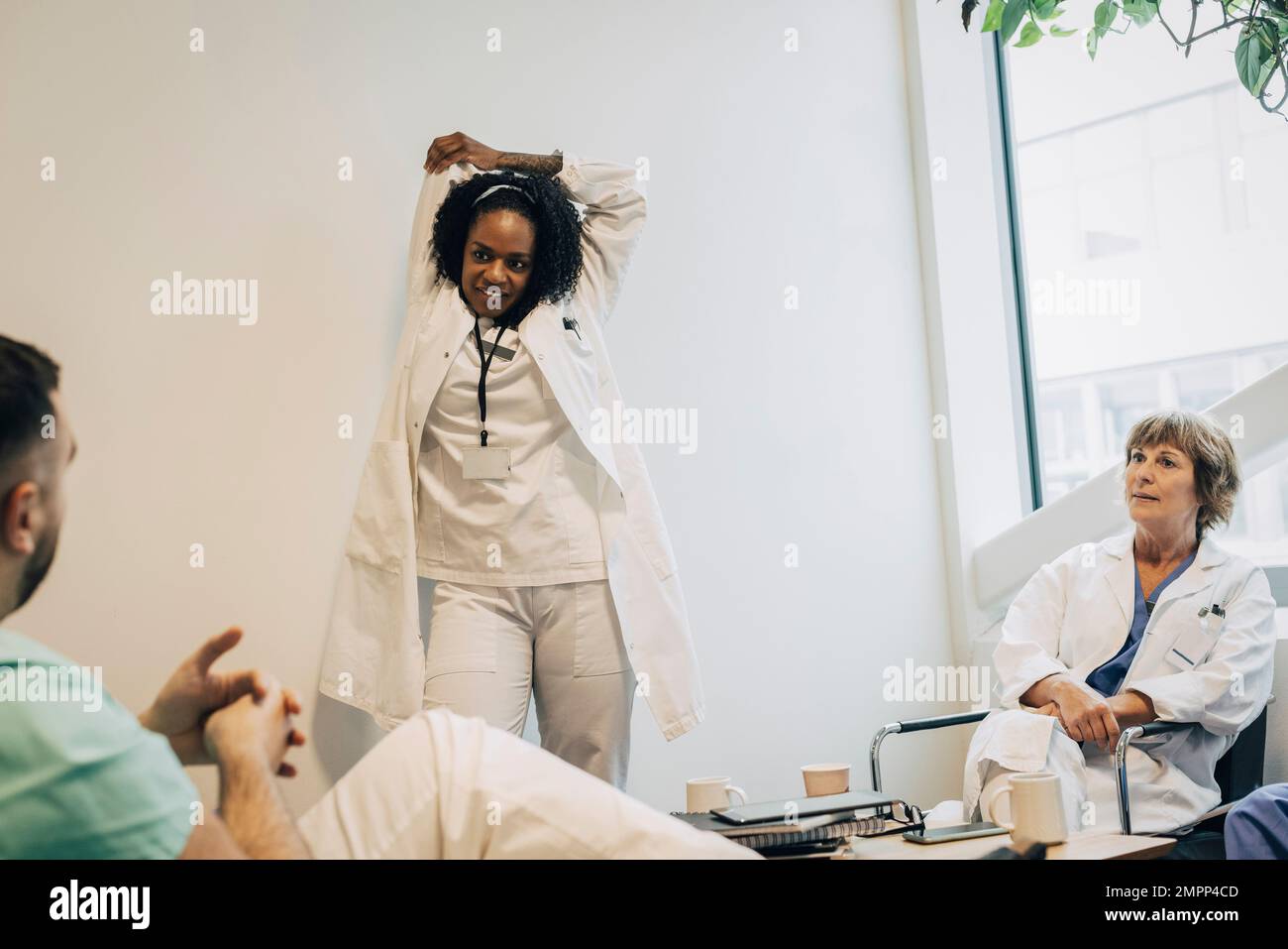 Female doctor stretching while talking with colleagues during coffee ...