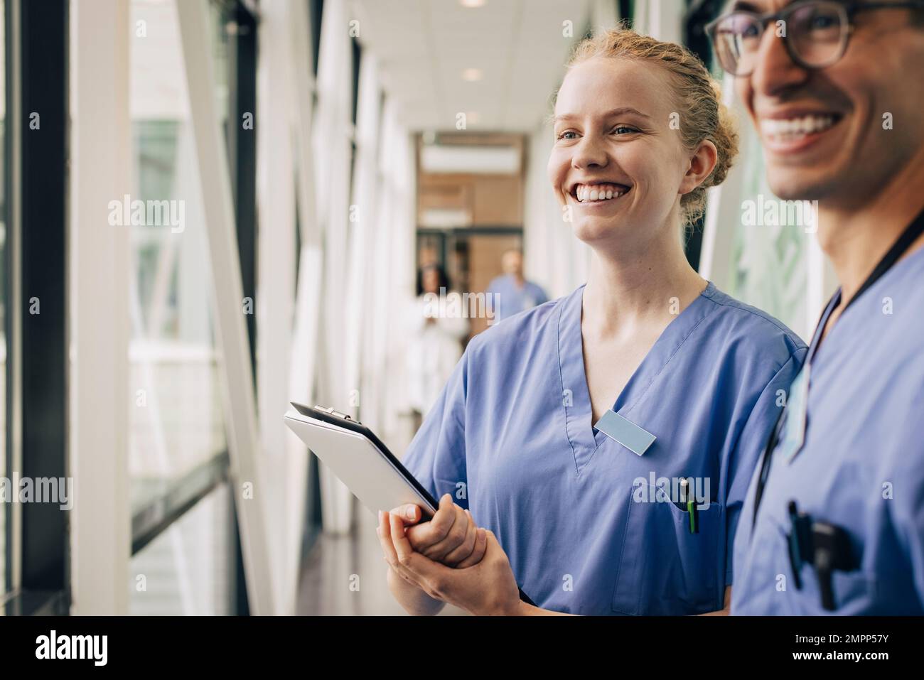 Happy female nurse looking away while holding clipboard at hospital ...