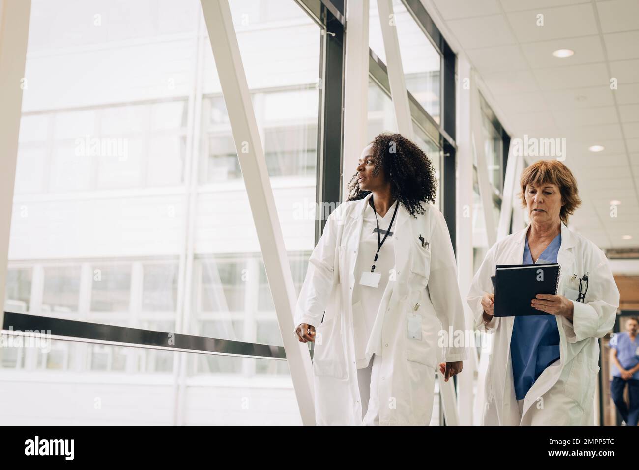 Mature female doctors walking by window in corridor at hospital Stock ...