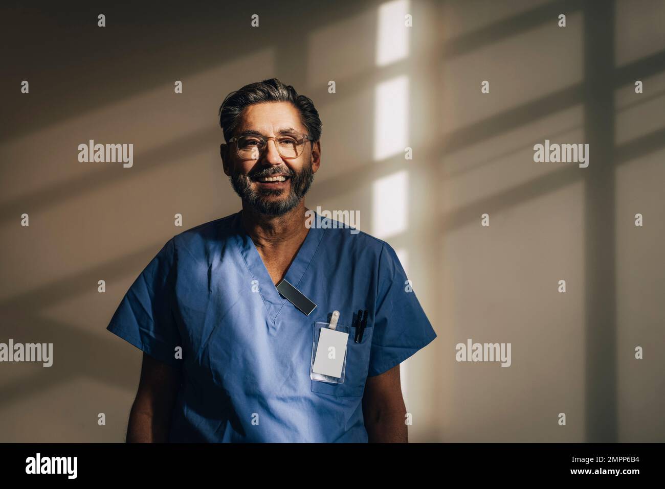 Portrait of happy male doctor standing against wall at hospital Stock ...