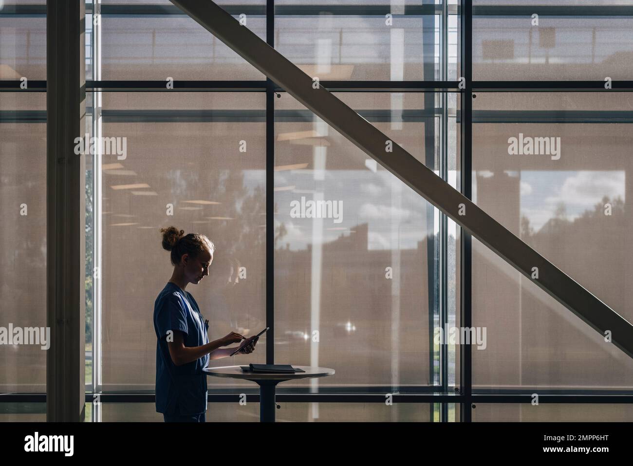 Side view of female nurse using tablet PC while standing by window at ...