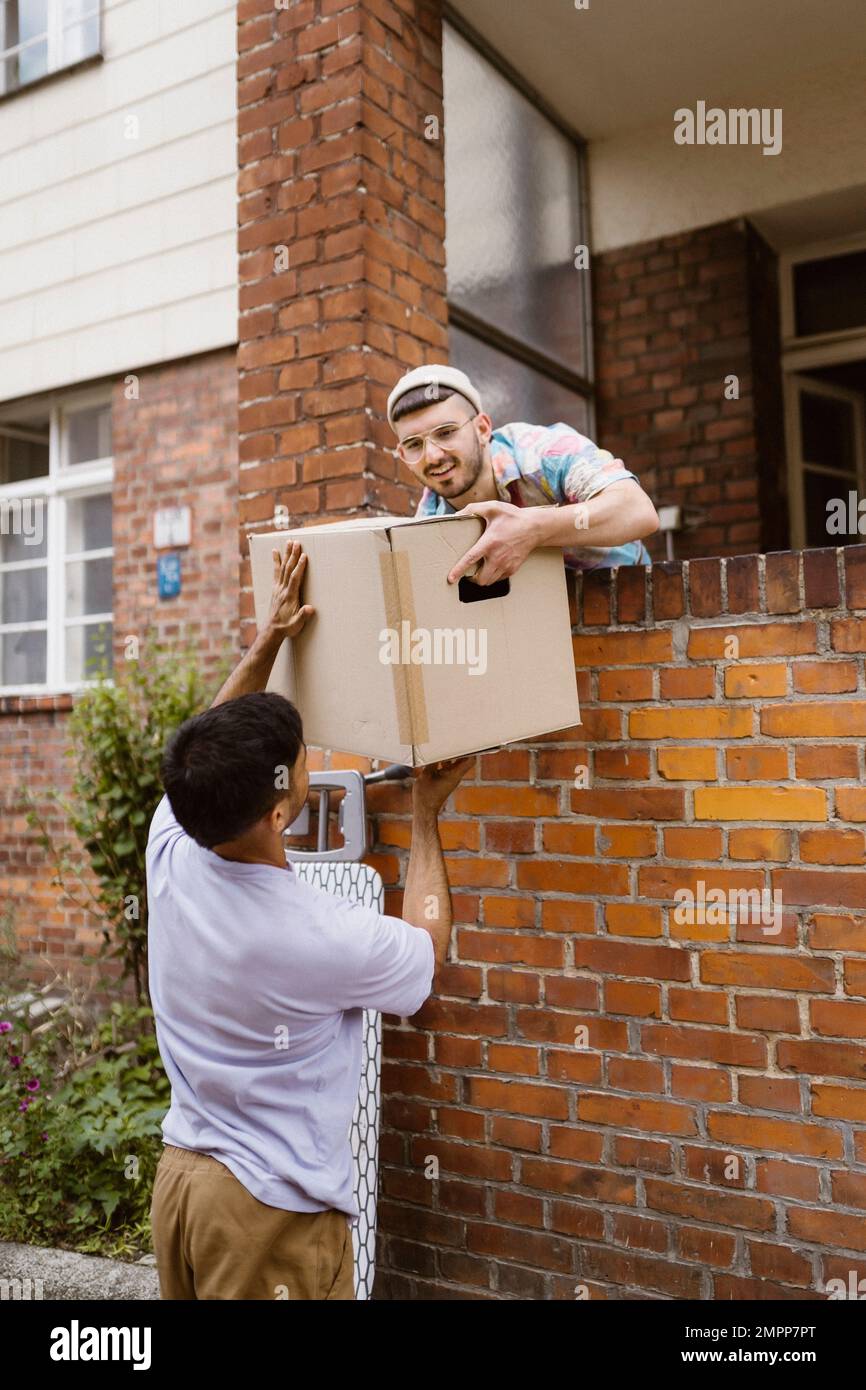 Gay couple helping each other while holding cardboard box over brick ...