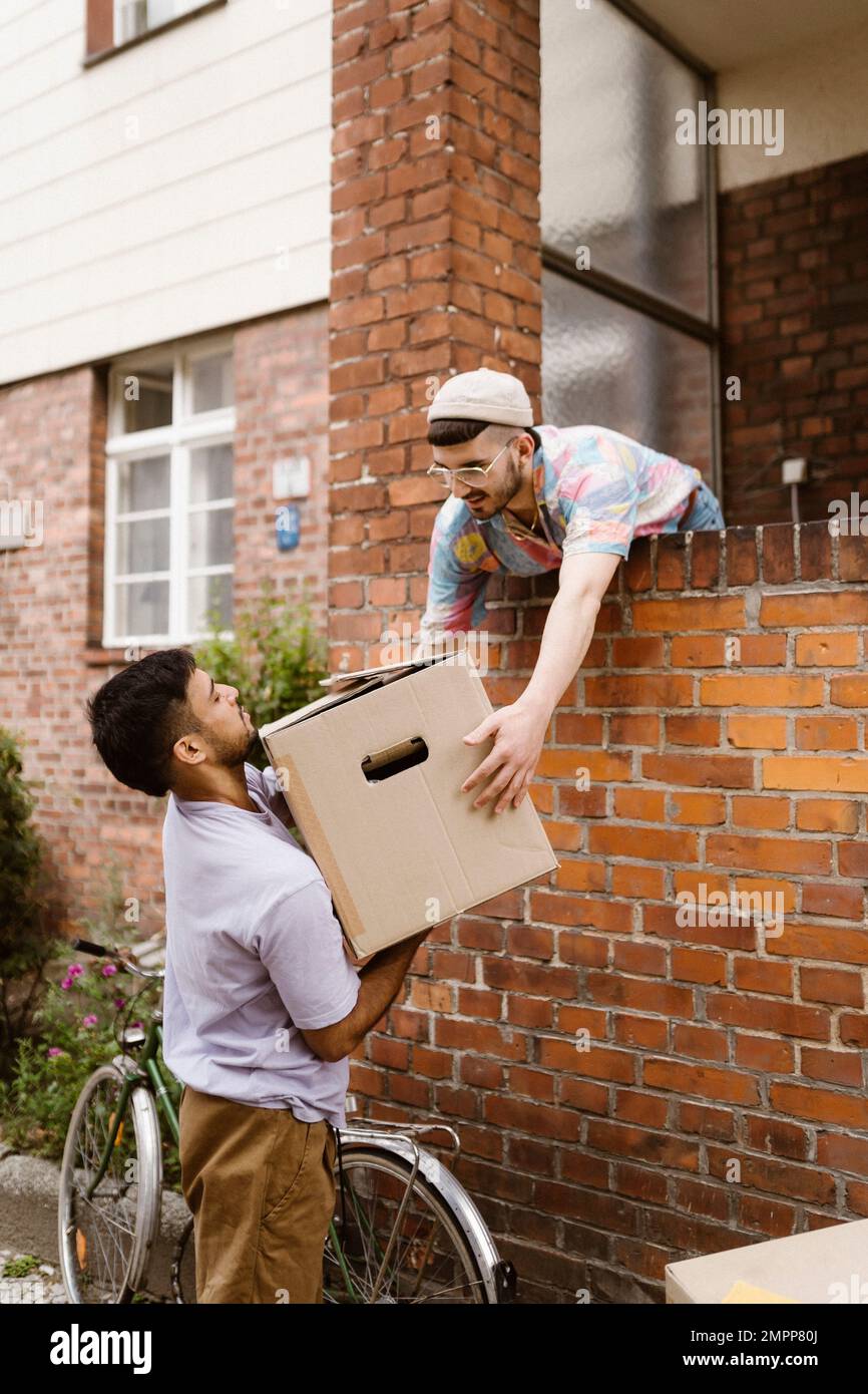 Man passing cardboard box to boyfriend while leaning on brick wall ...