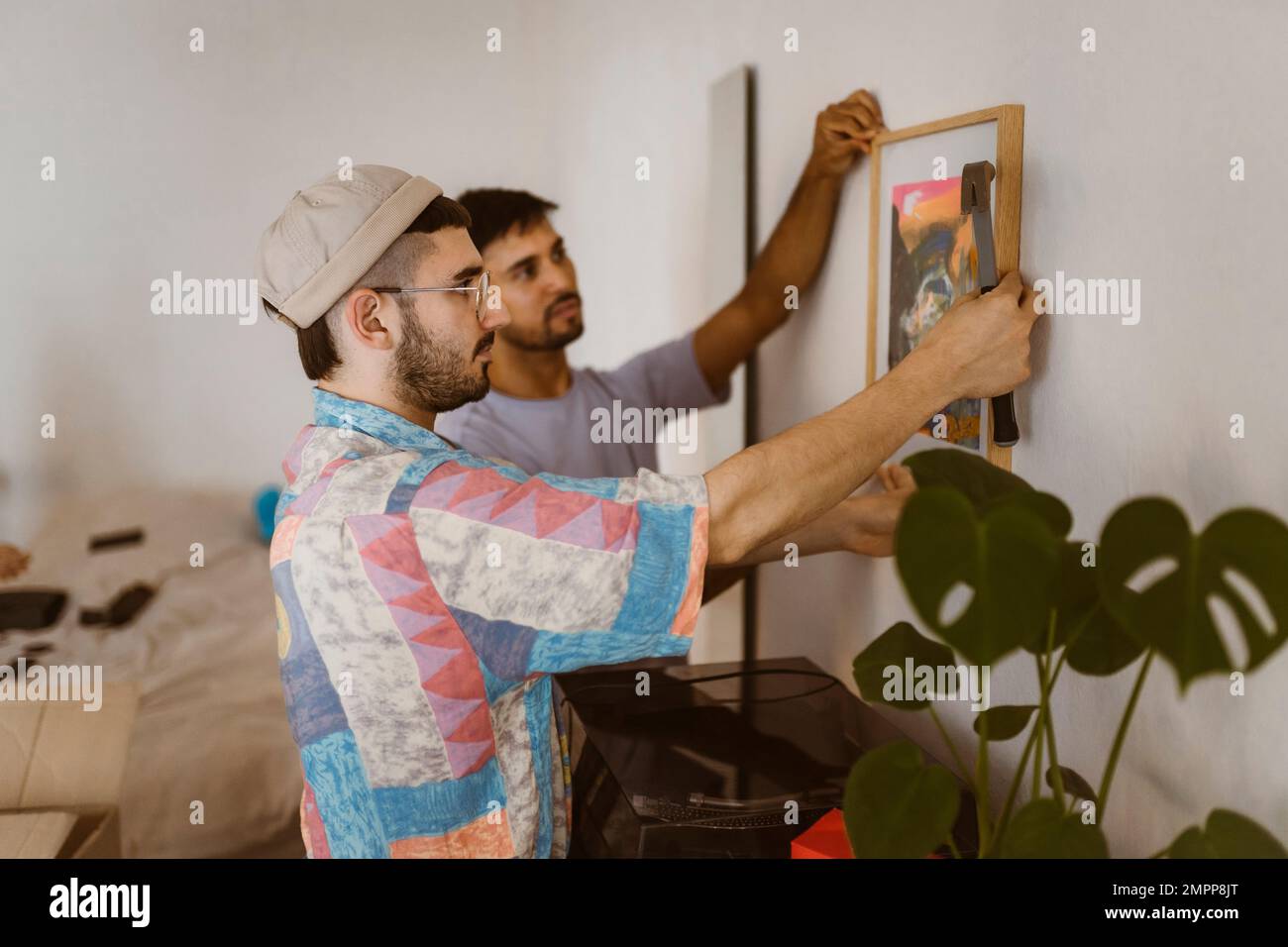Side view of man hanging frame on wall with boyfriend at home Stock ...