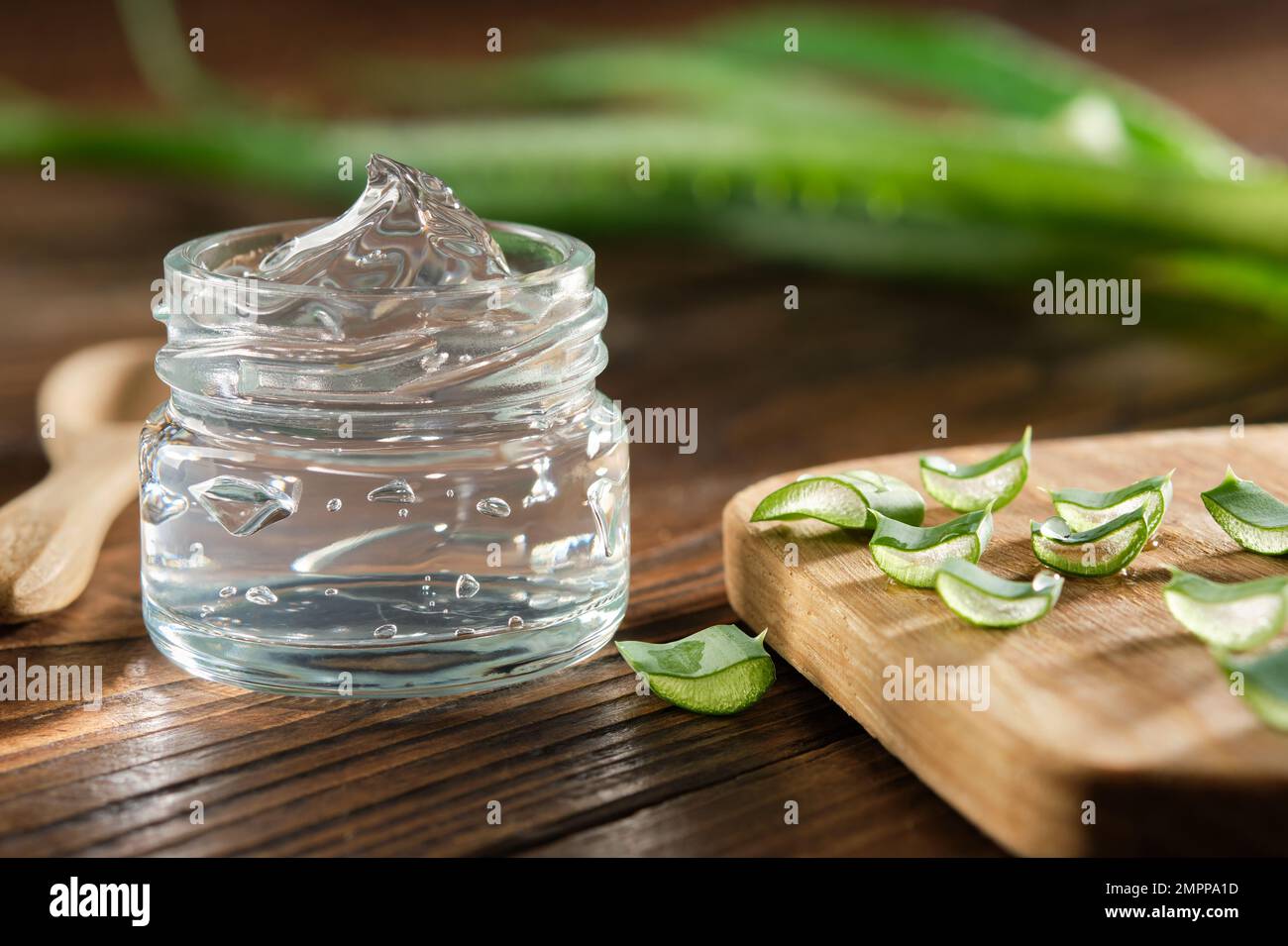 Transparent glass jar of aloe vera gel, sliced aloe leaves on a cutting ...