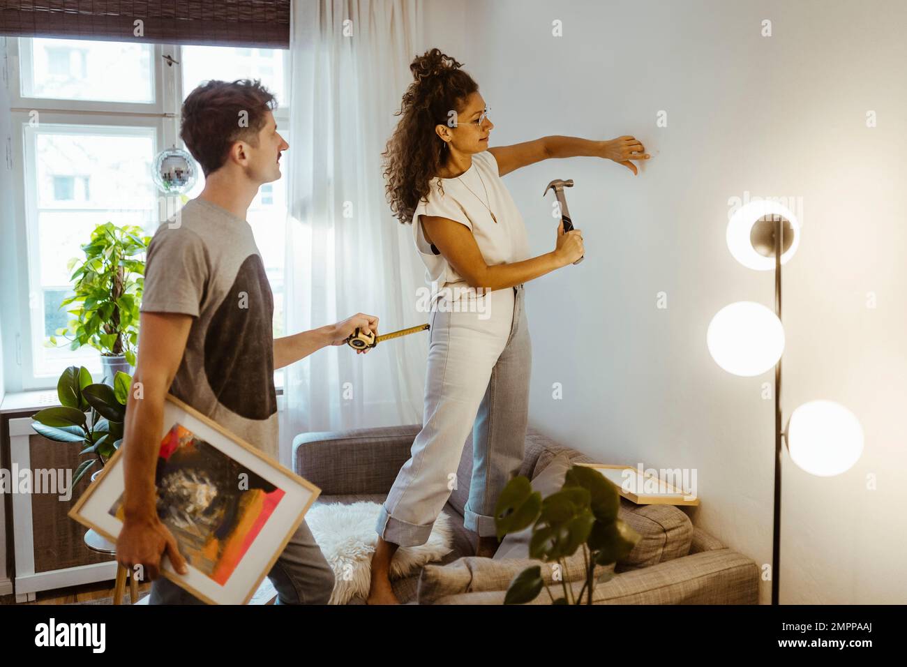 Woman hammering nail in wall with boyfriend holding picture frame and ...