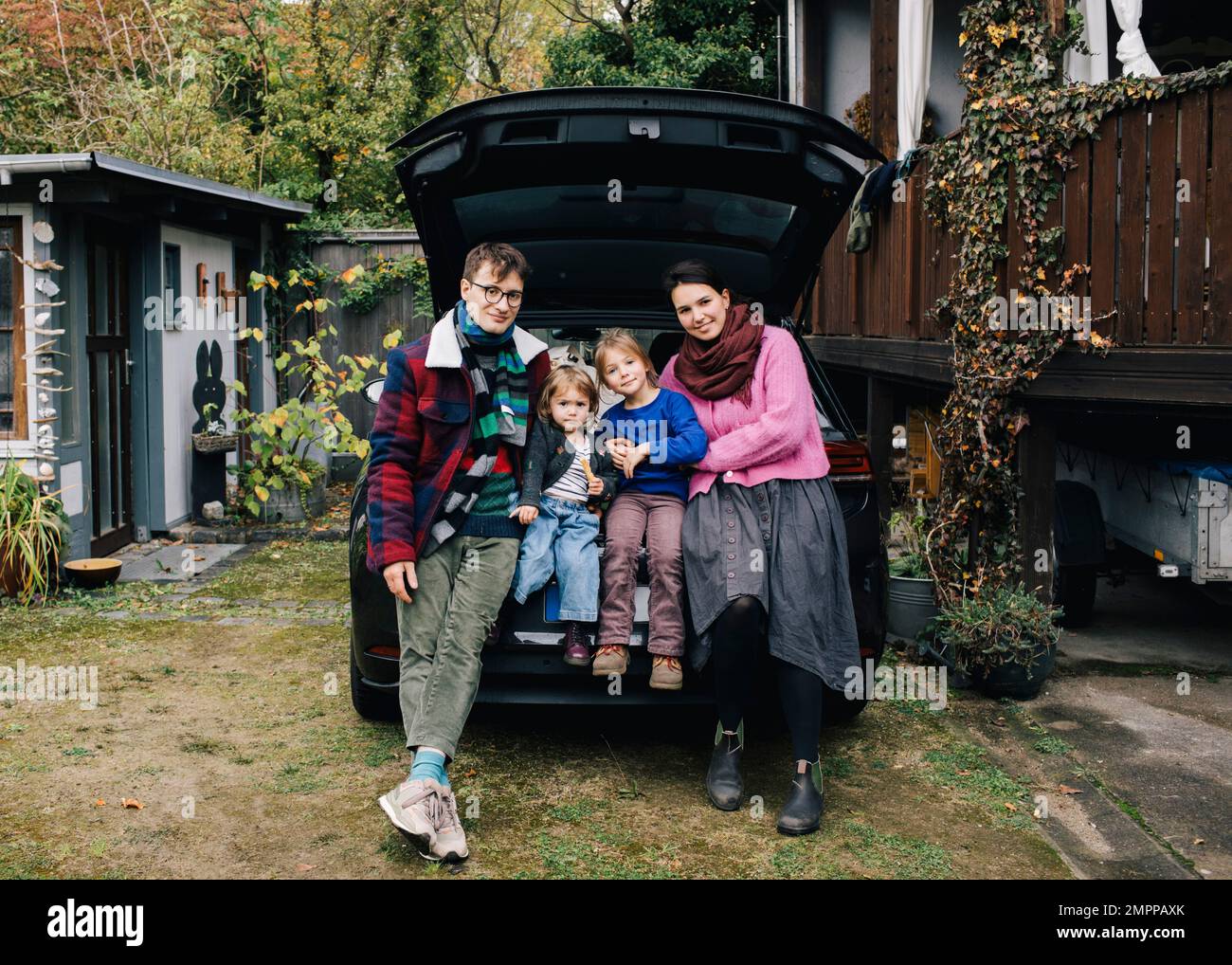 Smiling family sitting together in car trunk outside house Stock Photo ...