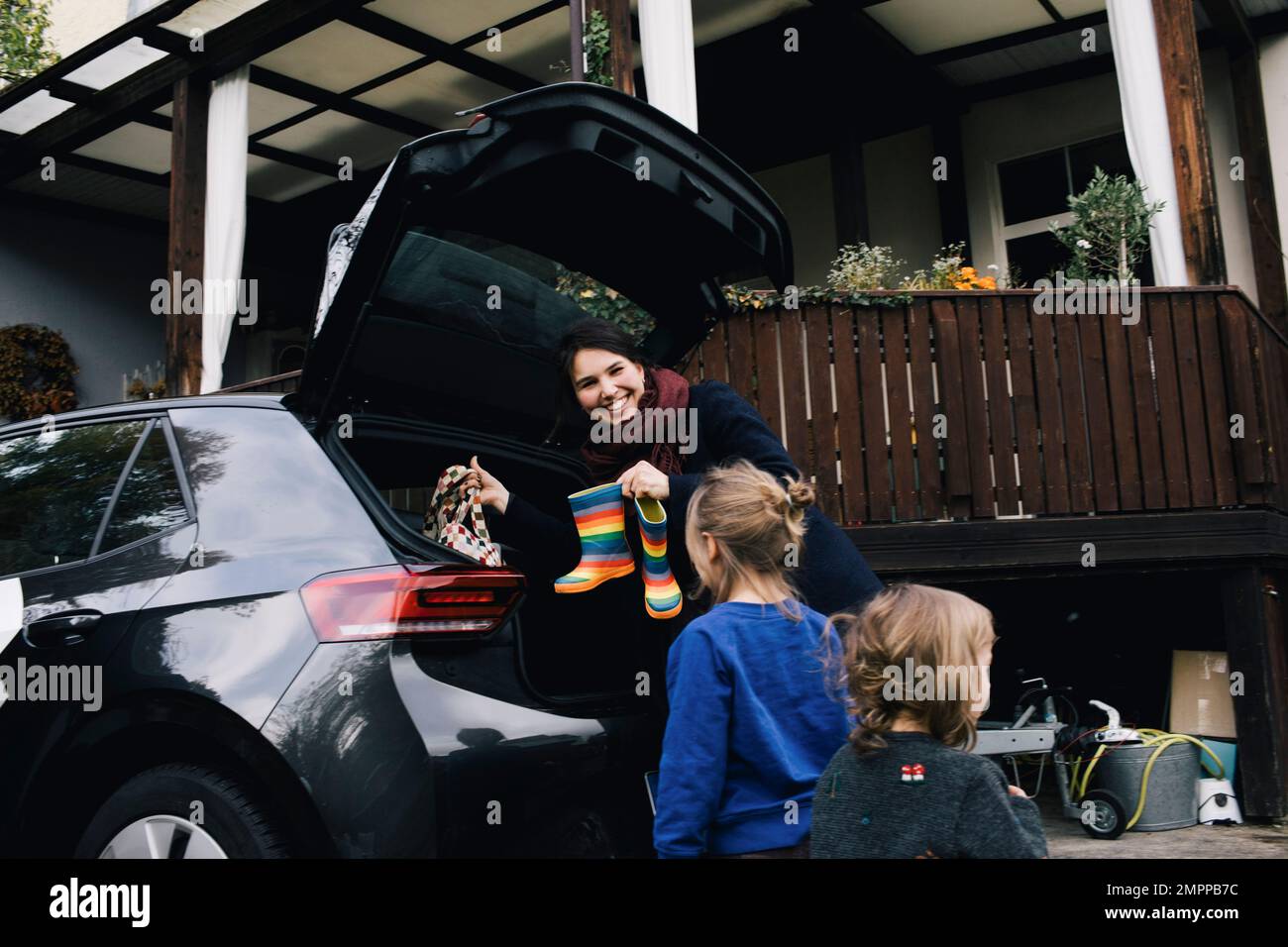 Happy mother with daughters loading boots and bag in trunk of electric ...