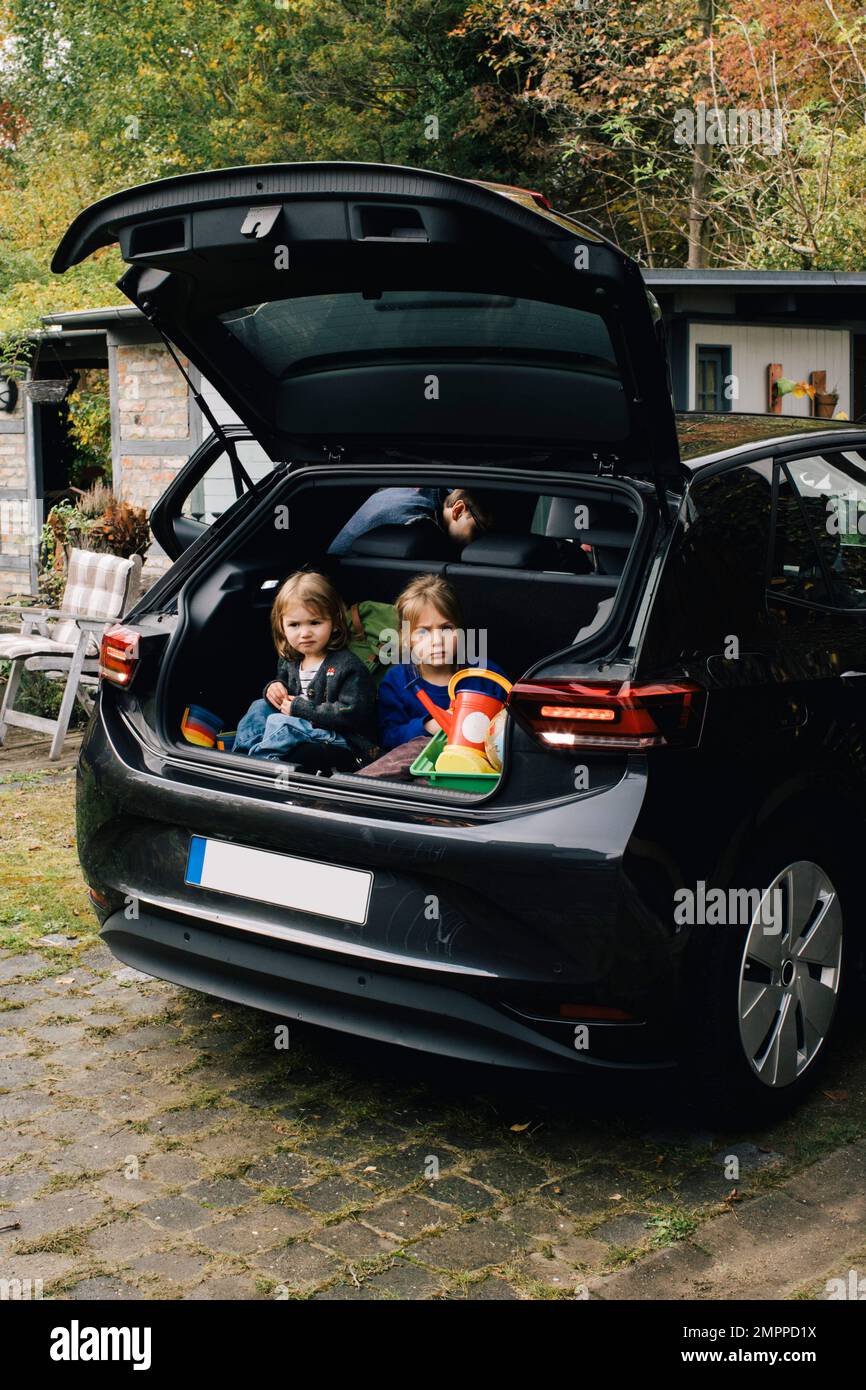 Sisters sitting in electric car trunk parked outside house Stock Photo ...