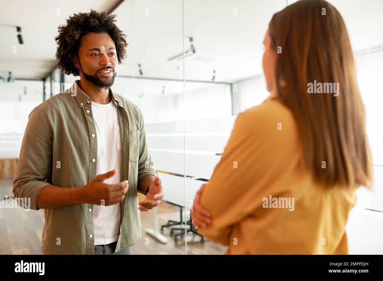 Two coworkers chatting during coffee break standing in glass hall of ...