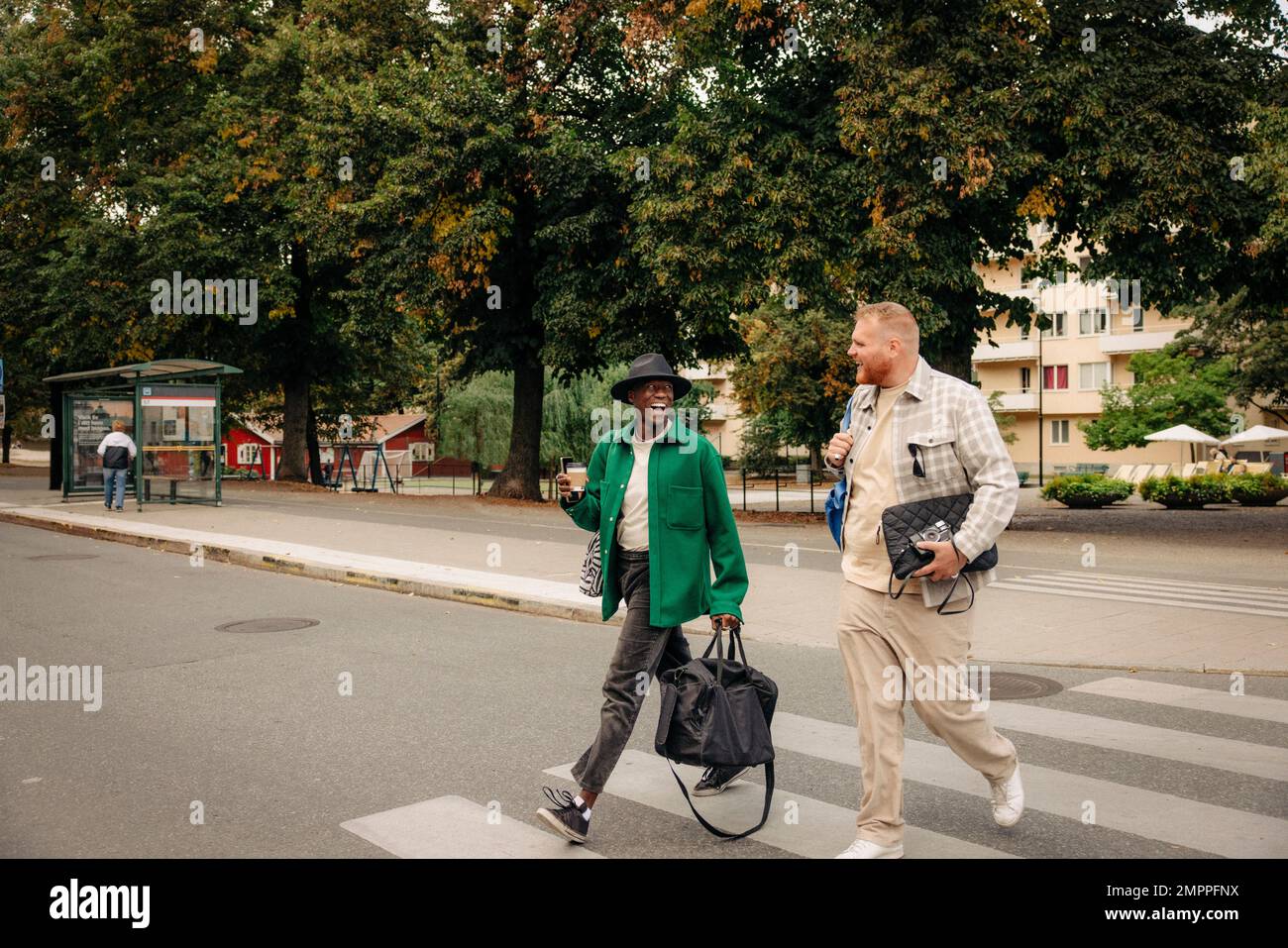 Happy male friends talking to each other while crossing road in city ...