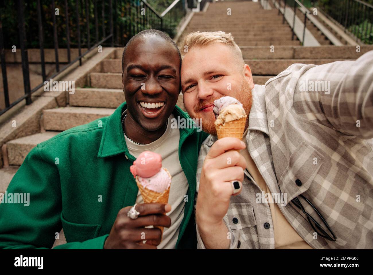 Happy male friends taking selfie while holding ice creams on steps ...