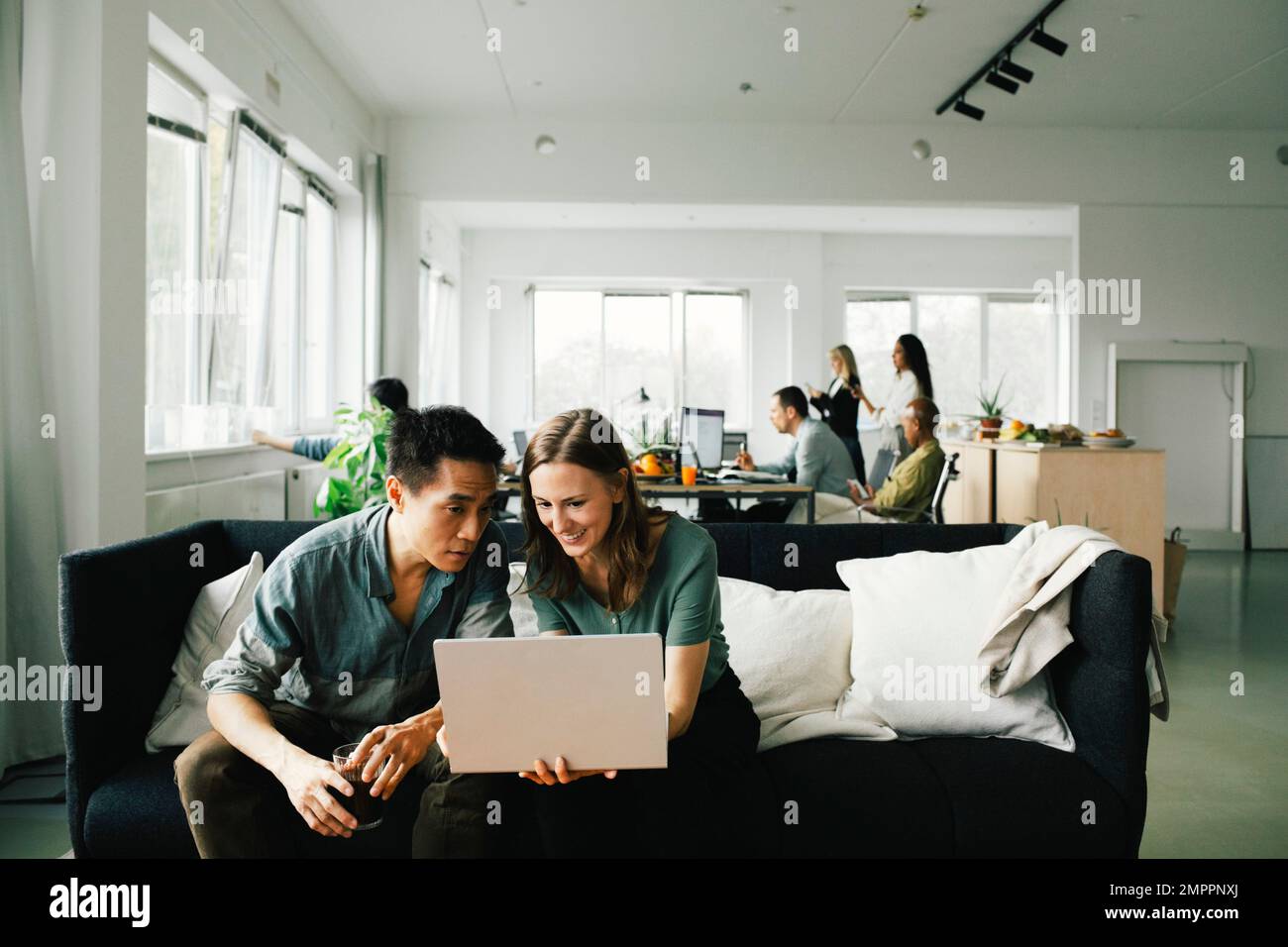 Multiracial business colleagues sharing laptop while sitting on sofa at ...