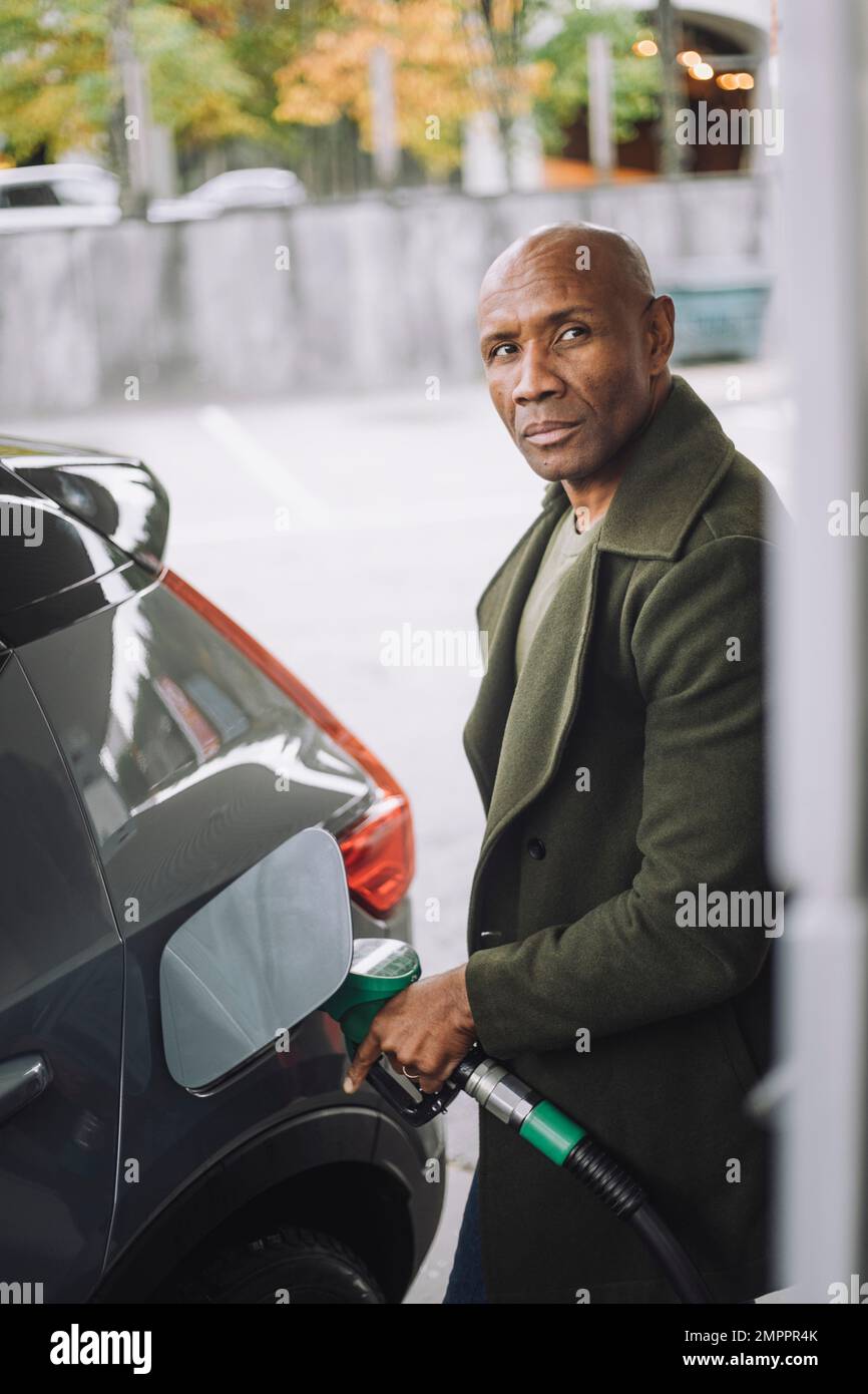 Mature man with shaved head refueling car at fuel station Stock Photo ...