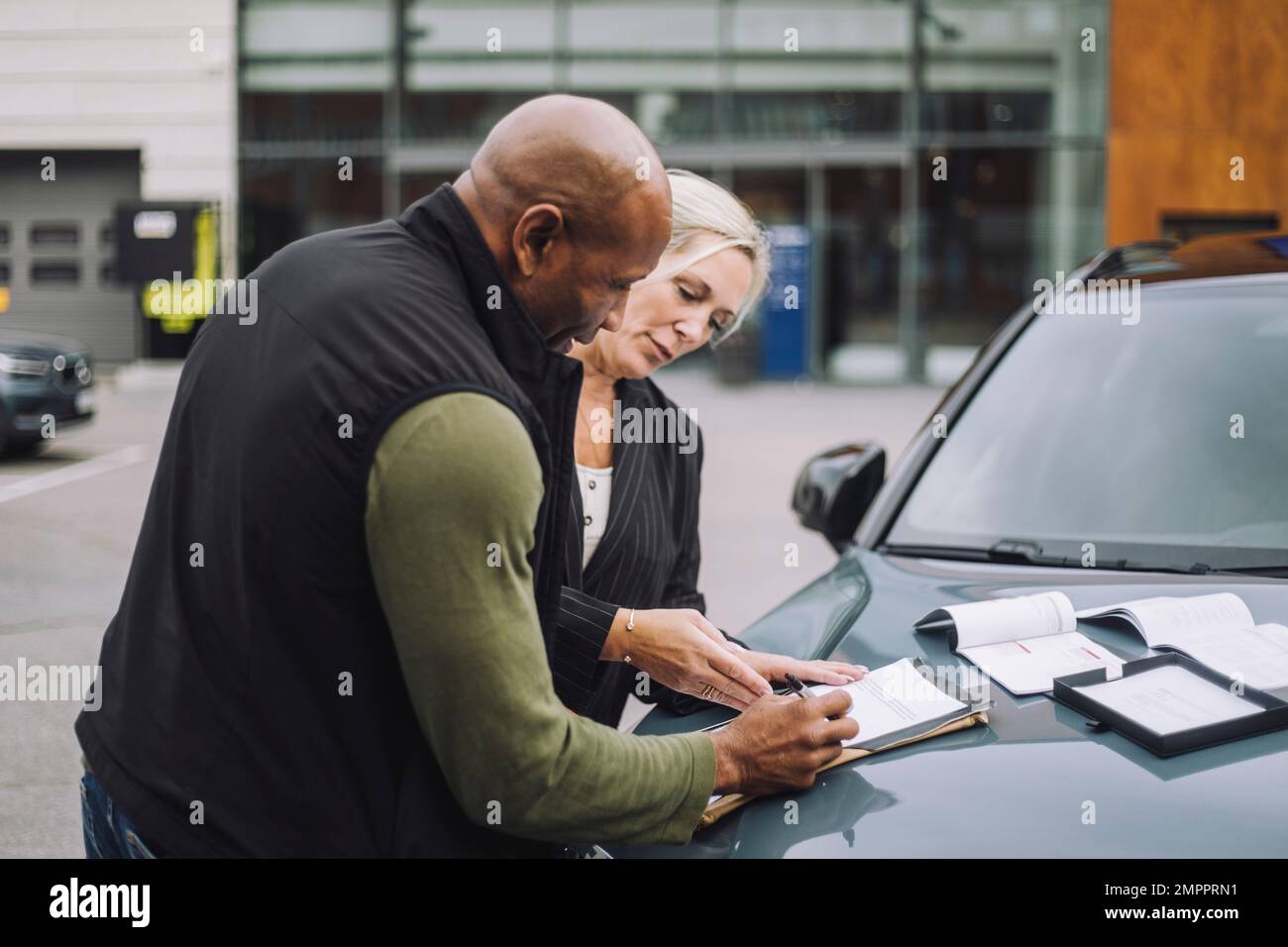 Saleswoman assisting male customer while doing paperwork standing near ...