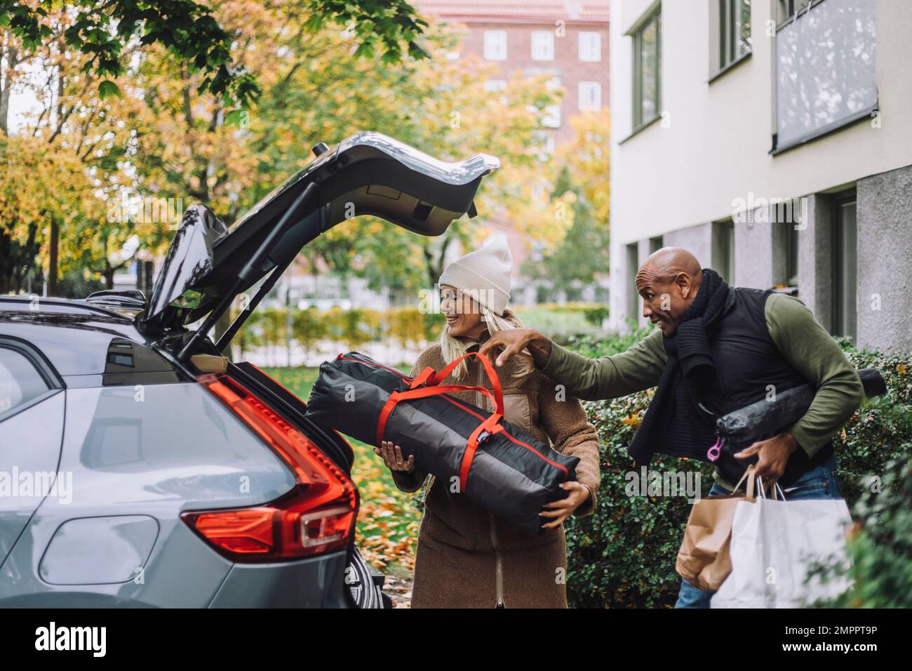 Man assisting woman loading luggage in car trunk while relocating house ...