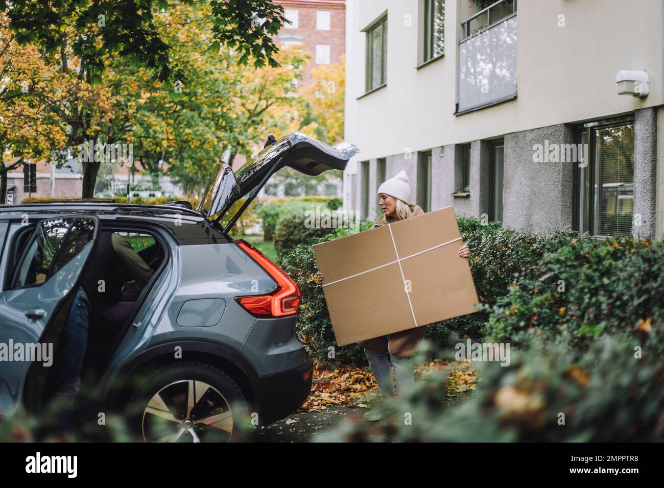 Woman walking towards car trunk carrying cardboard Stock Photo - Alamy