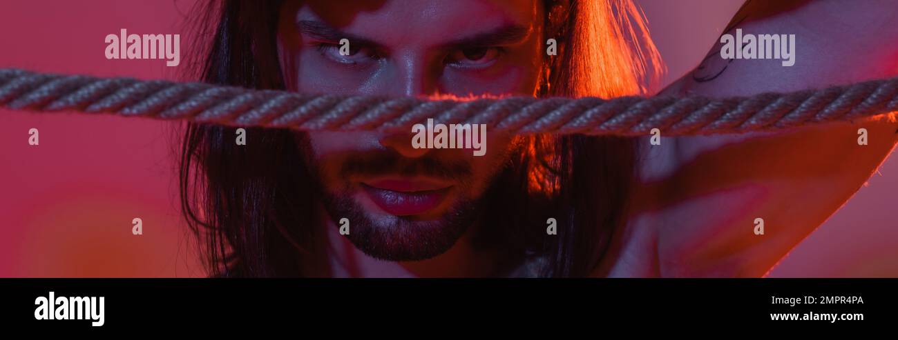 Long haired man looking at camera near rope on purple background with ...