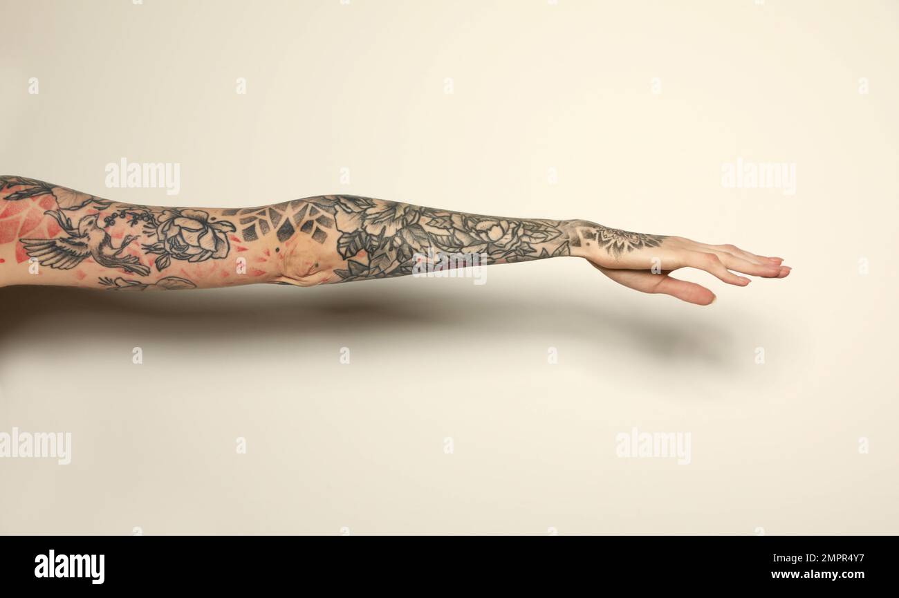 Woman with colorful tattoos on arm against white background, closeup ...