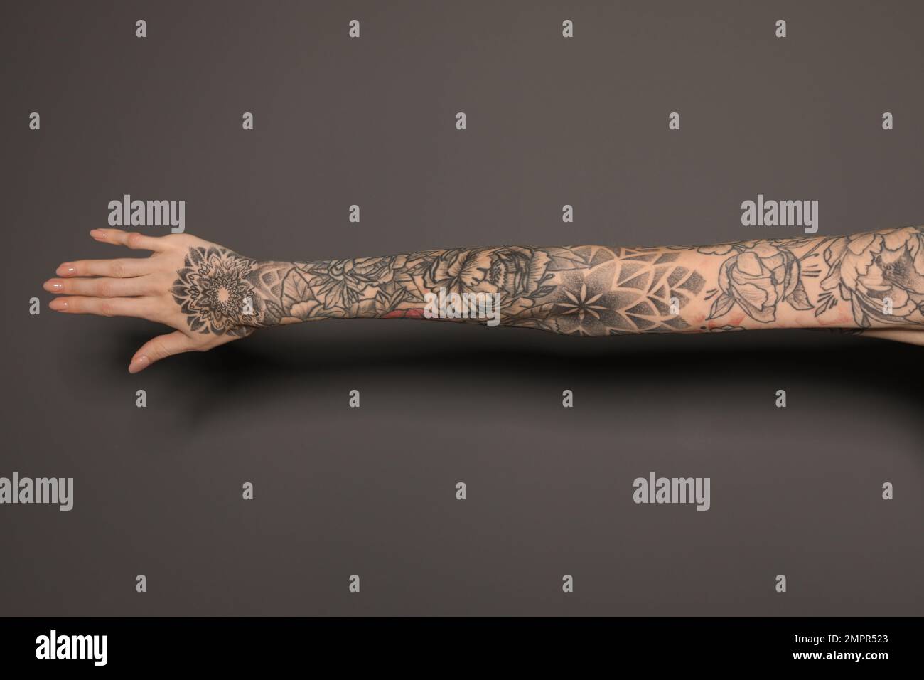 Woman with colorful tattoos on arm against dark grey background ...