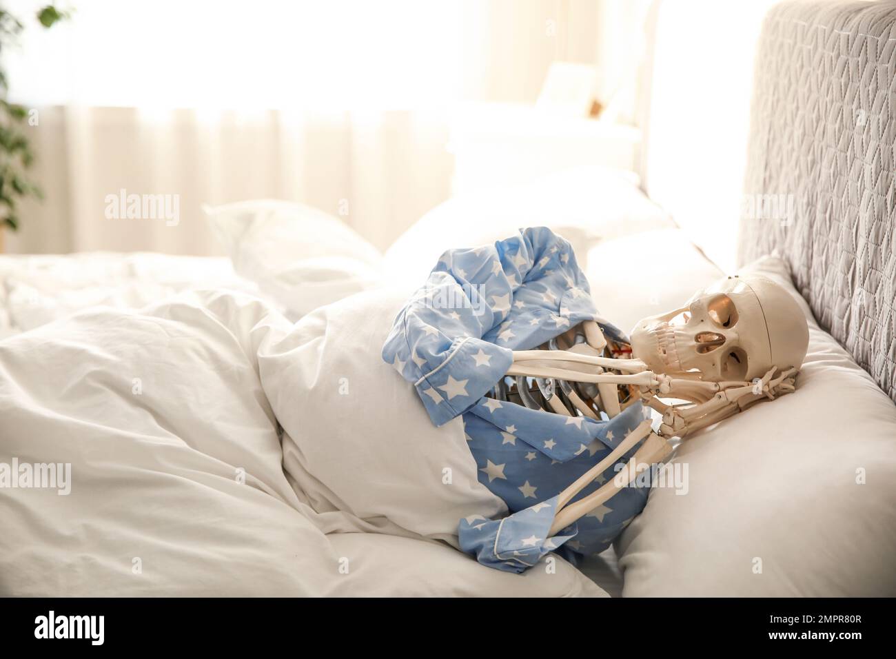 Human skeleton in pajamas lying on bed indoors Stock Photo - Alamy
