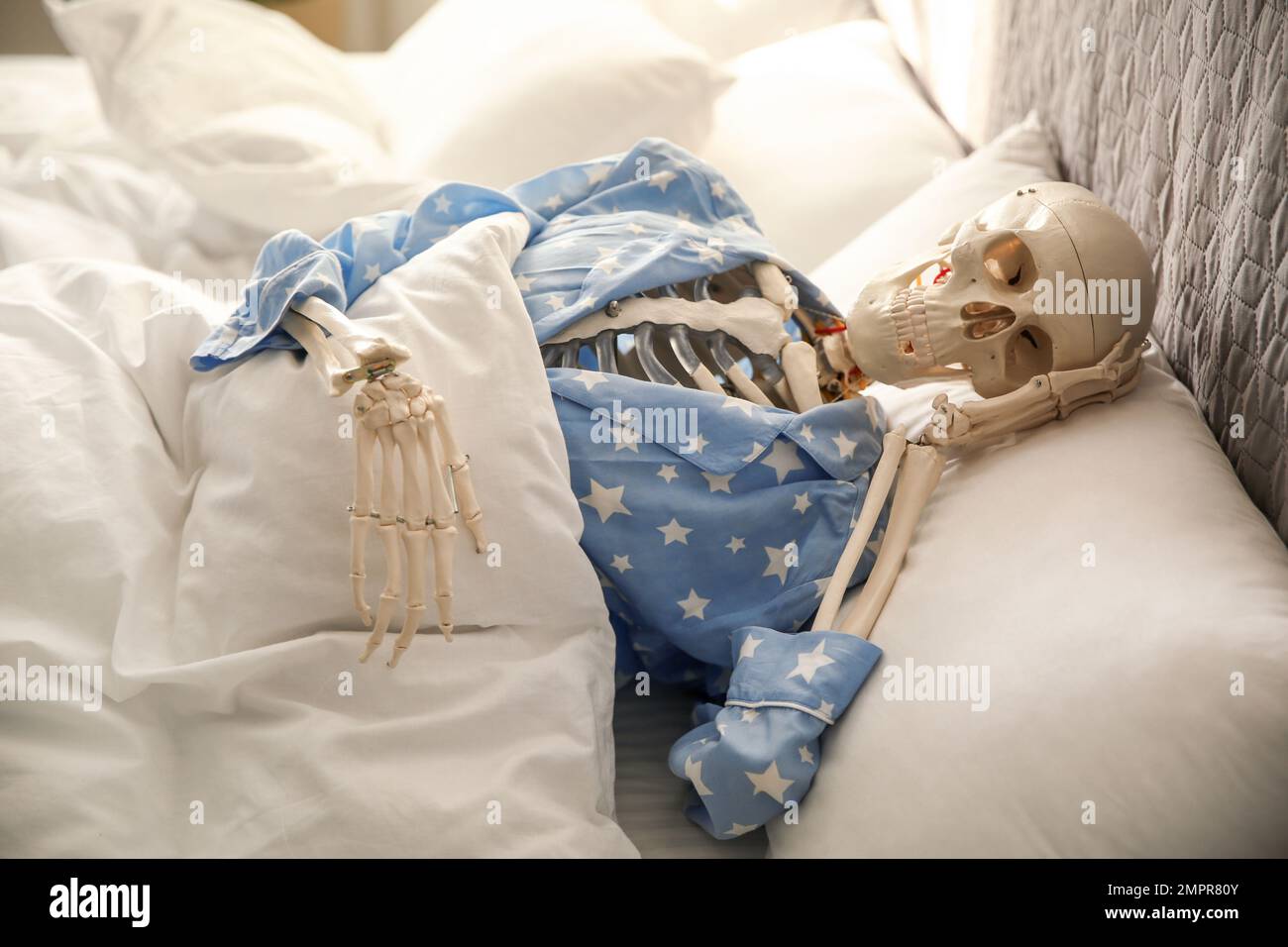 Human skeleton in pajamas lying on bed indoors Stock Photo - Alamy