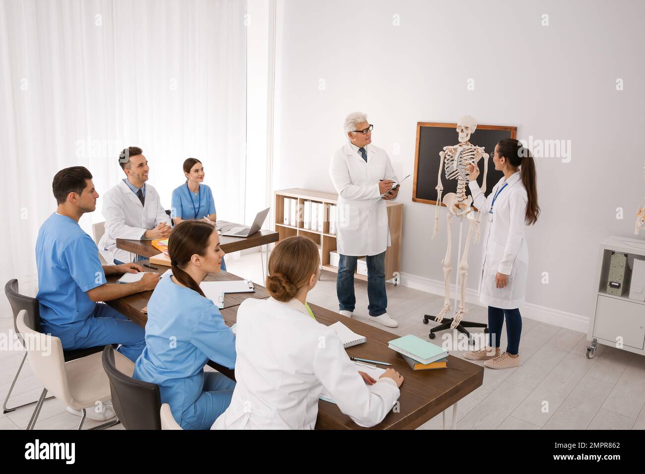 Medical students and professor studying human skeleton anatomy in ...