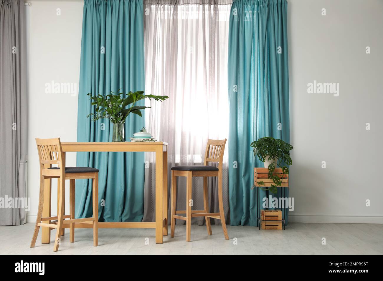 Stylish wooden table and chairs near window with elegant curtains in ...