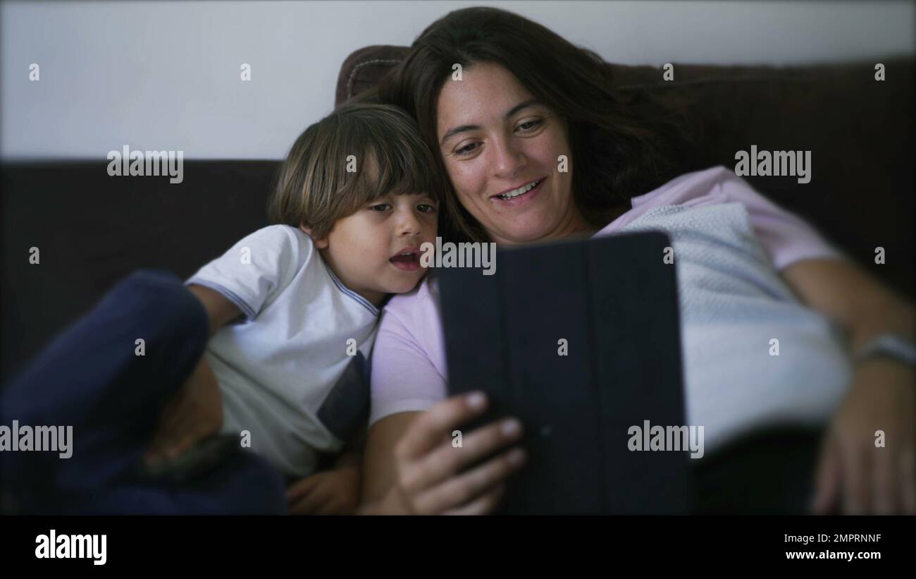 Mother and child looking at tablet device screen together on couch at ...