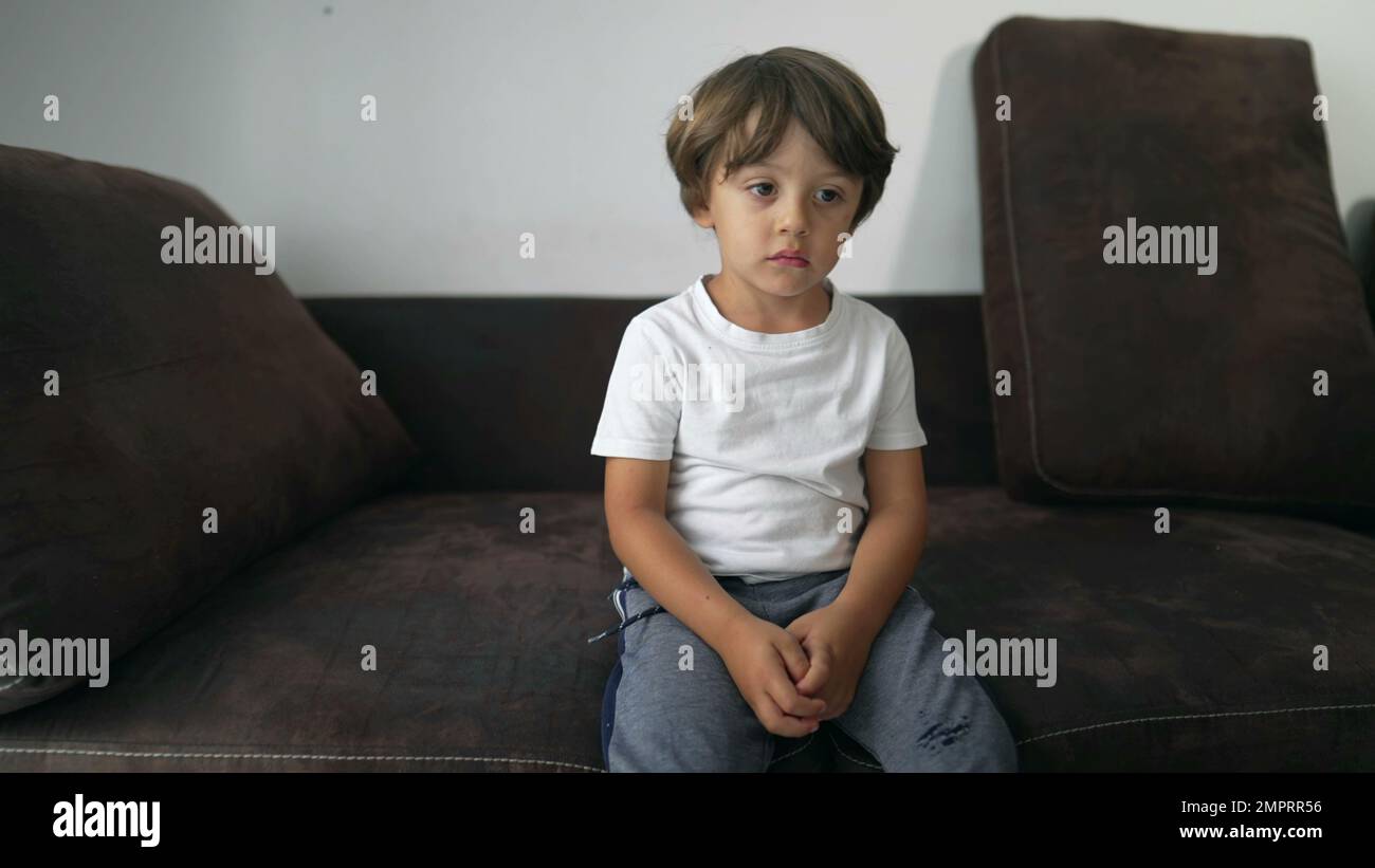 One bored child sitting on couch at home with nothing to do. Young boy ...