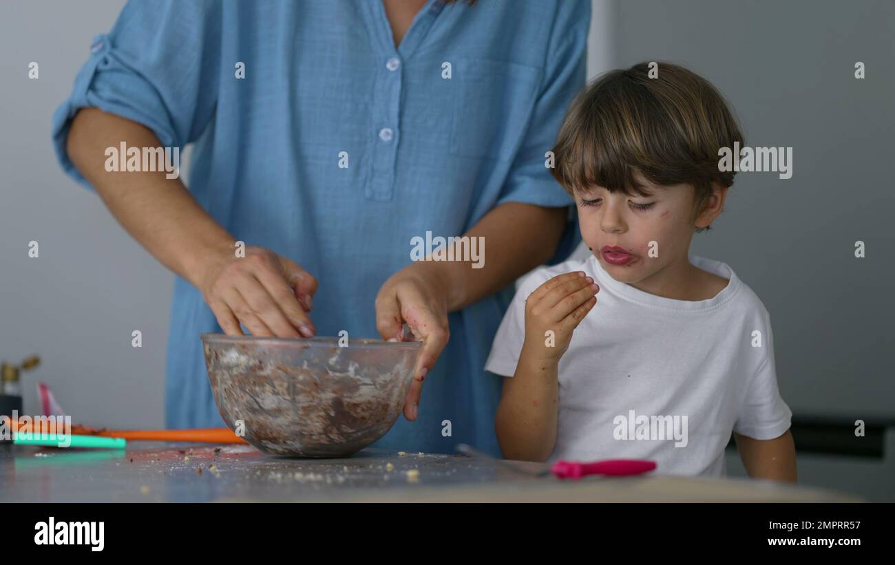 Mother mixing ingredients by hand with child eating dough. Parent and ...