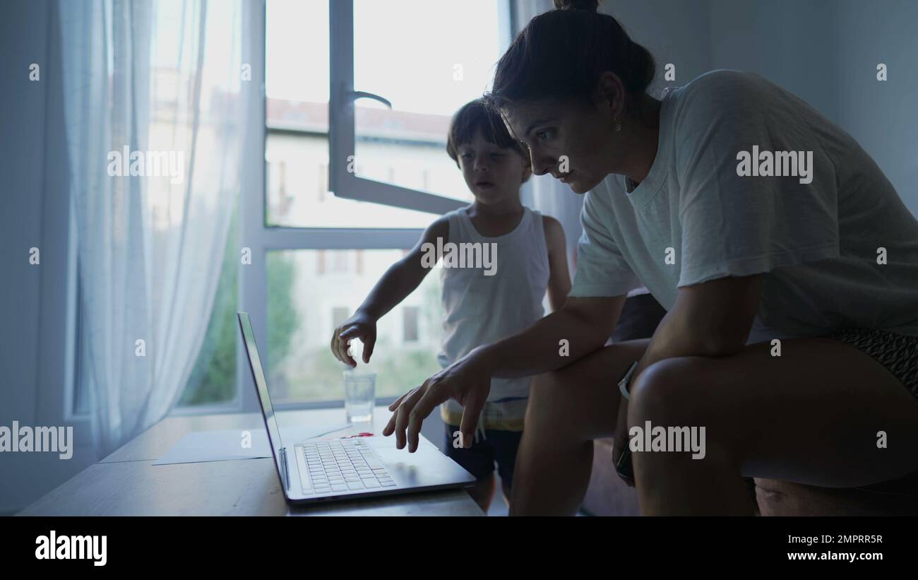 Mother browsing internet on laptop next to child. Candid mom using ...