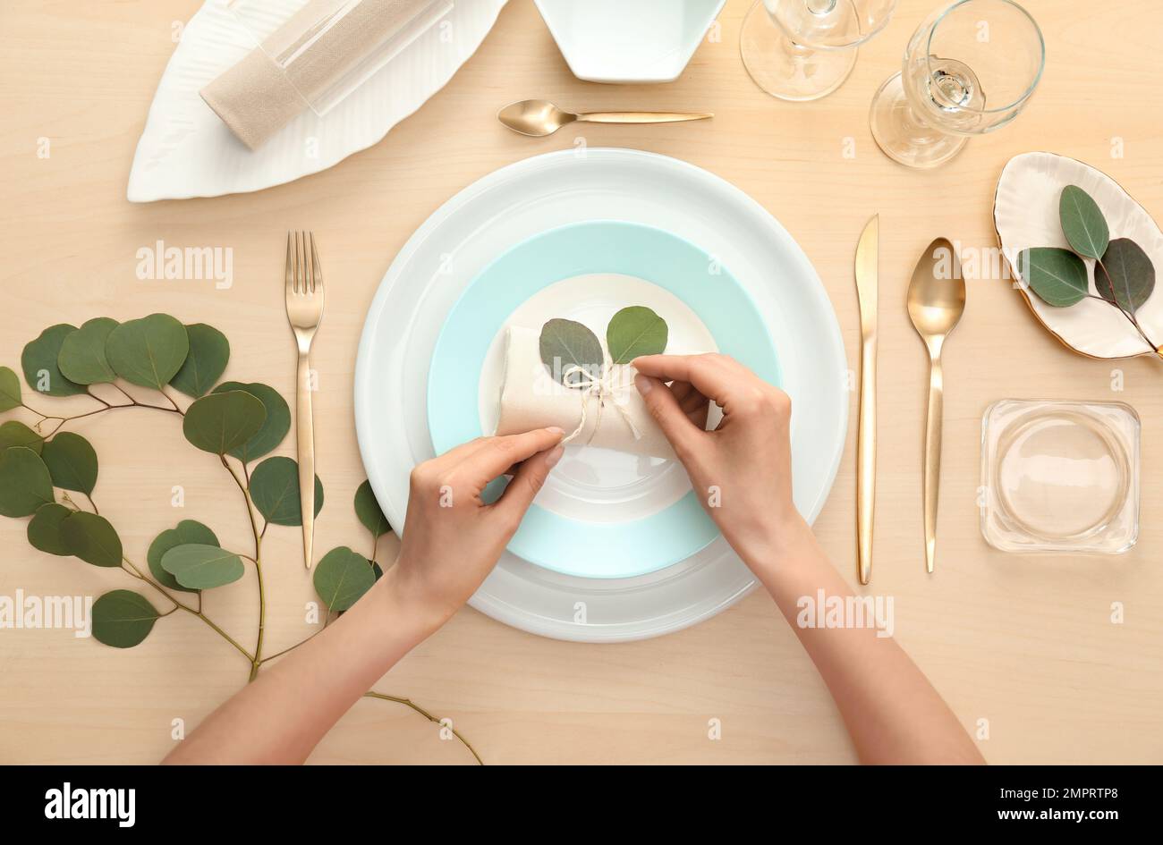 Woman setting table with green leaves for festive dinner, top view ...