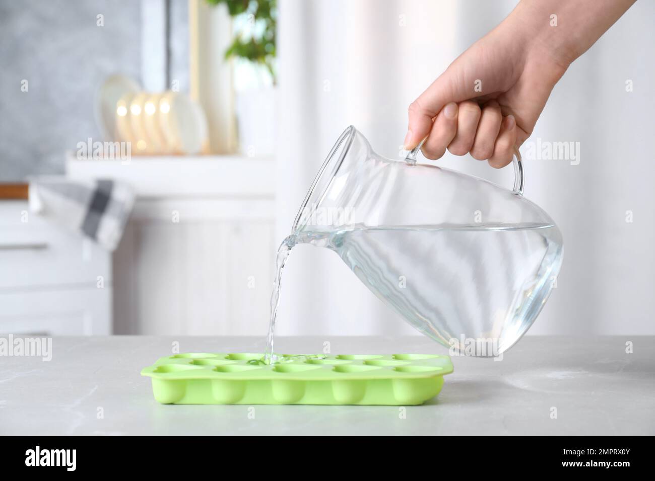 Woman pouring water into ice cube tray at grey marble table, closeup Stock Photo - Alamy