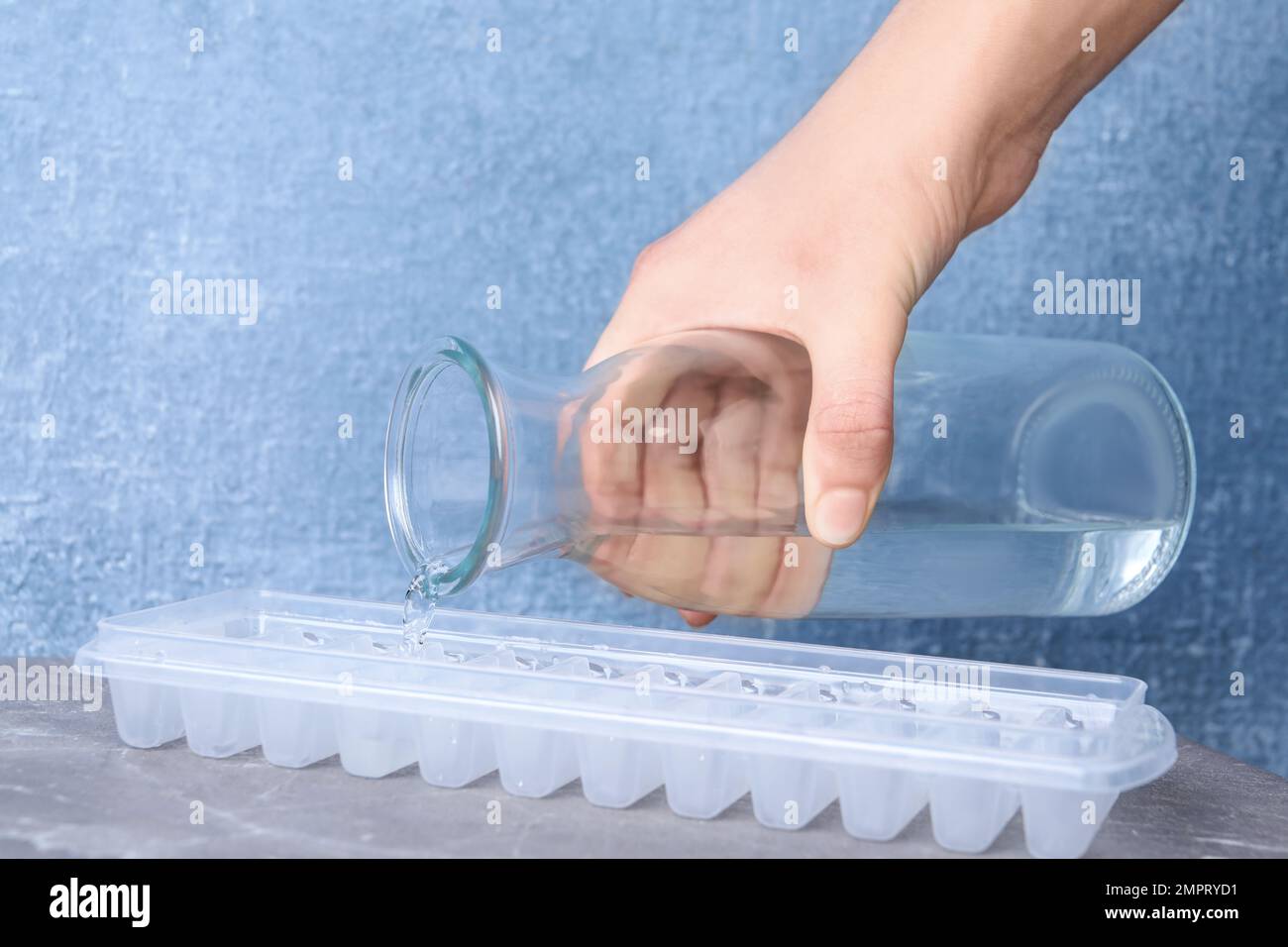 Woman pouring water into ice cube tray at light grey marble table, closeup Stock Photo - Alamy