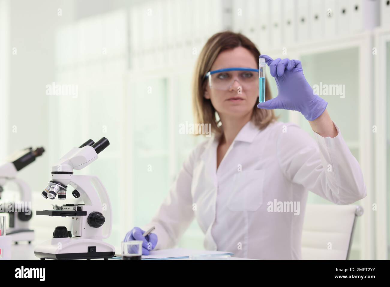 Woman chemist looking at test tube with blue liquid in front of ...