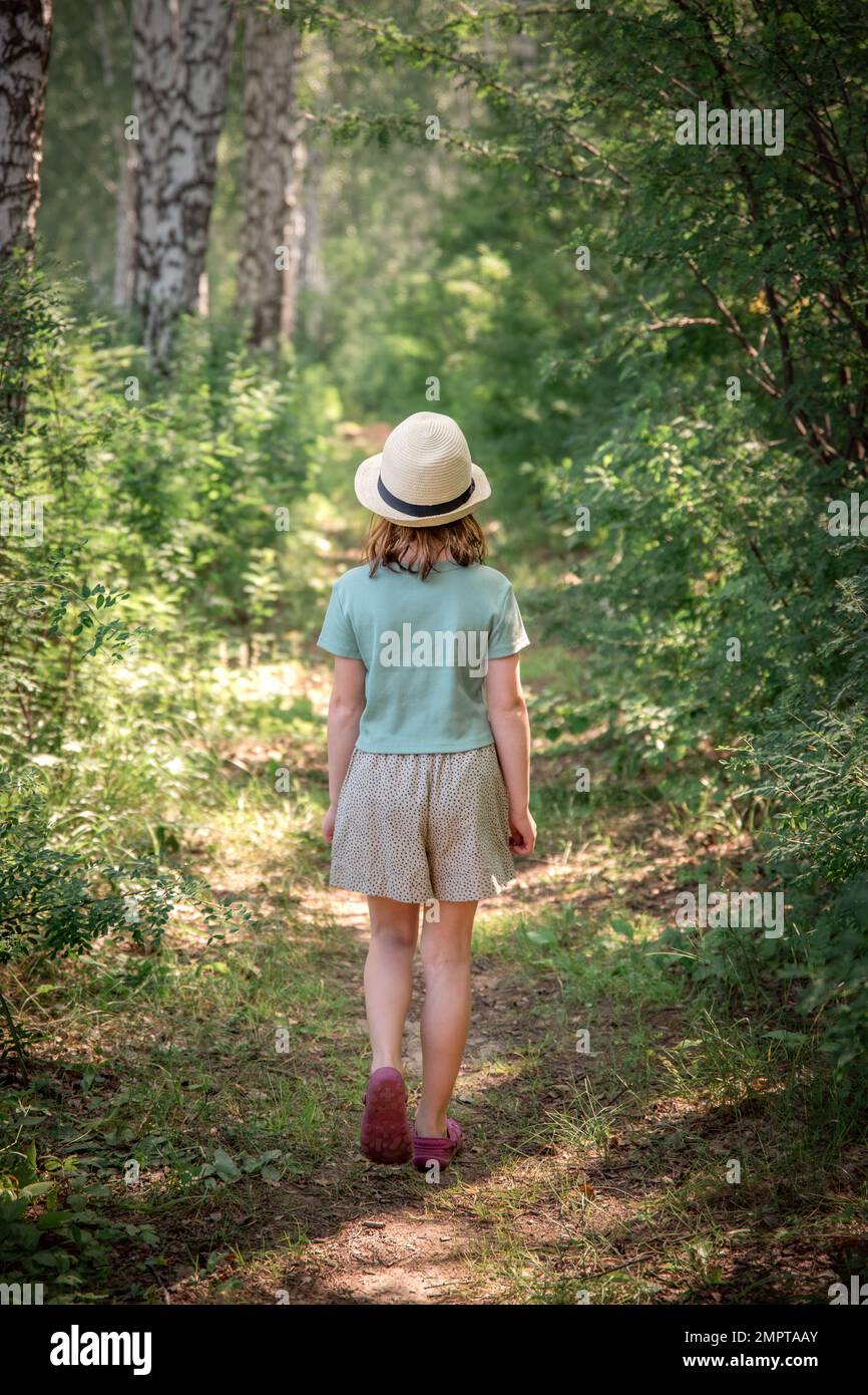 a cute girl in a straw hat walks along a path in the woods in the ...