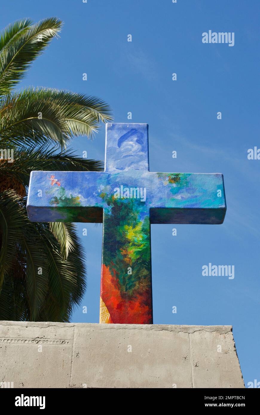 A crucifix with a rainbow pattern juxtaposed against a bright blue sky ...