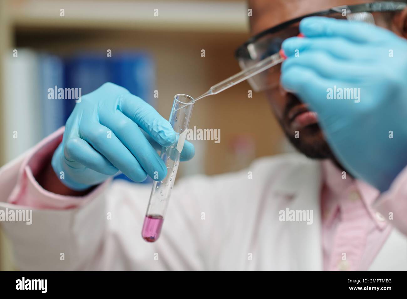 Researcher using pipette when dropping reagent in test-tube with pink ...