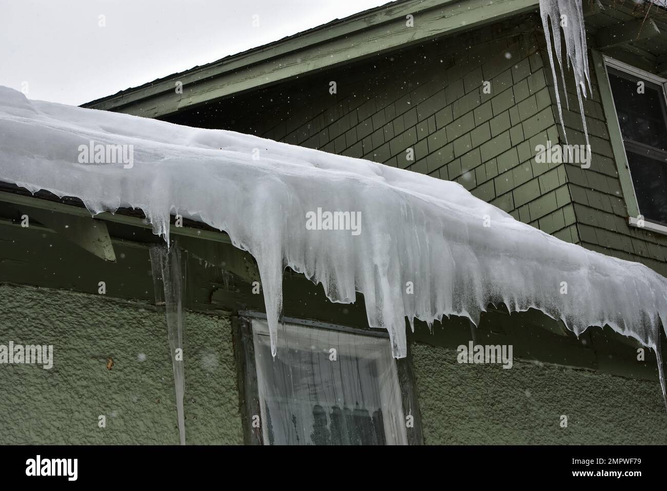 Melting snow on roof causing ice dam in gutter with icicles forming ...