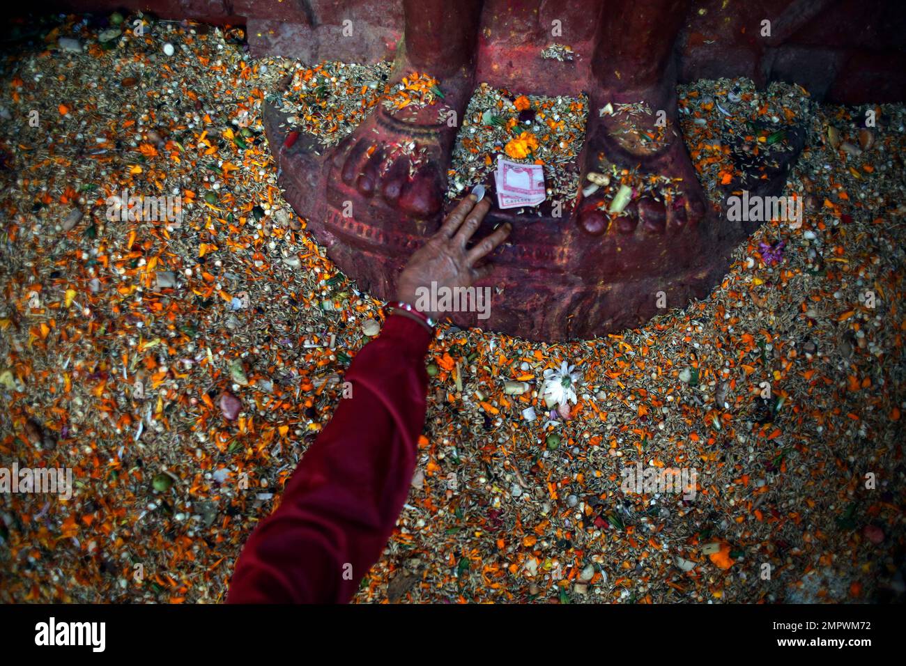 A devotee places a coin as an offering at the feet of a statue of God ...