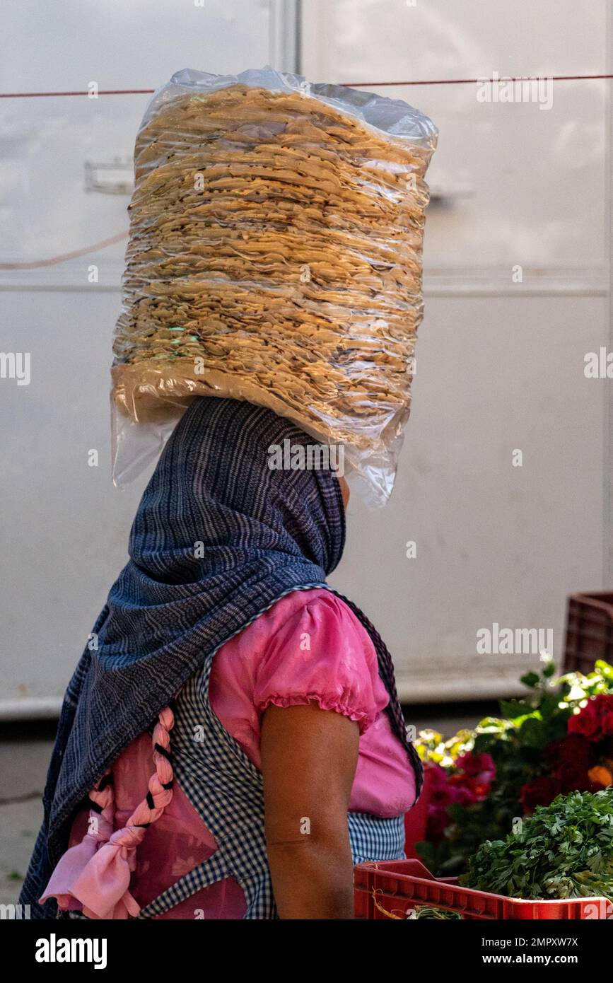 An indigenous Zapotec woman balances a large stack of tlayuda tortillas on her head in the ...