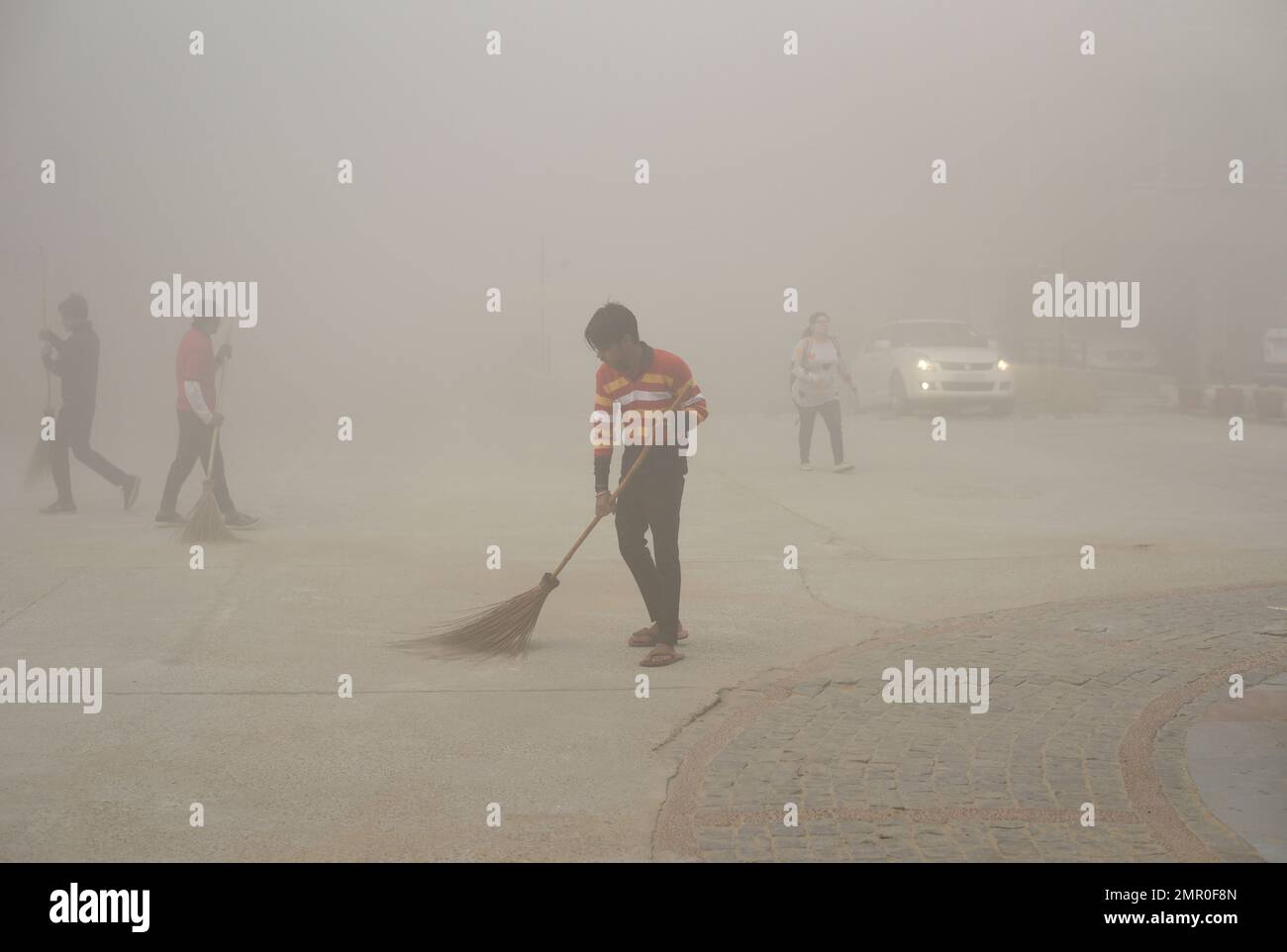 Indian workers use brooms to sweep away dust in the morning fog in ...