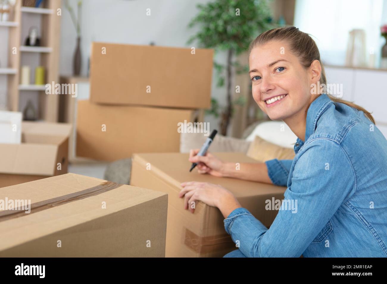 beautiful young woman marking a cardboard box and smiling Stock Photo ...