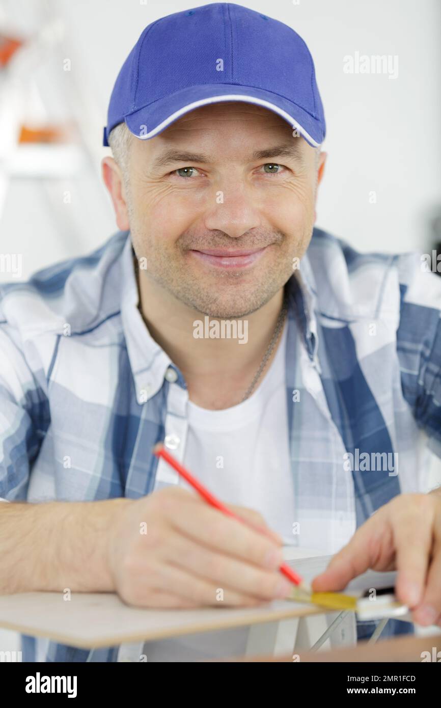 carpenter with pencil and folding rule while measuring wood workpiece ...