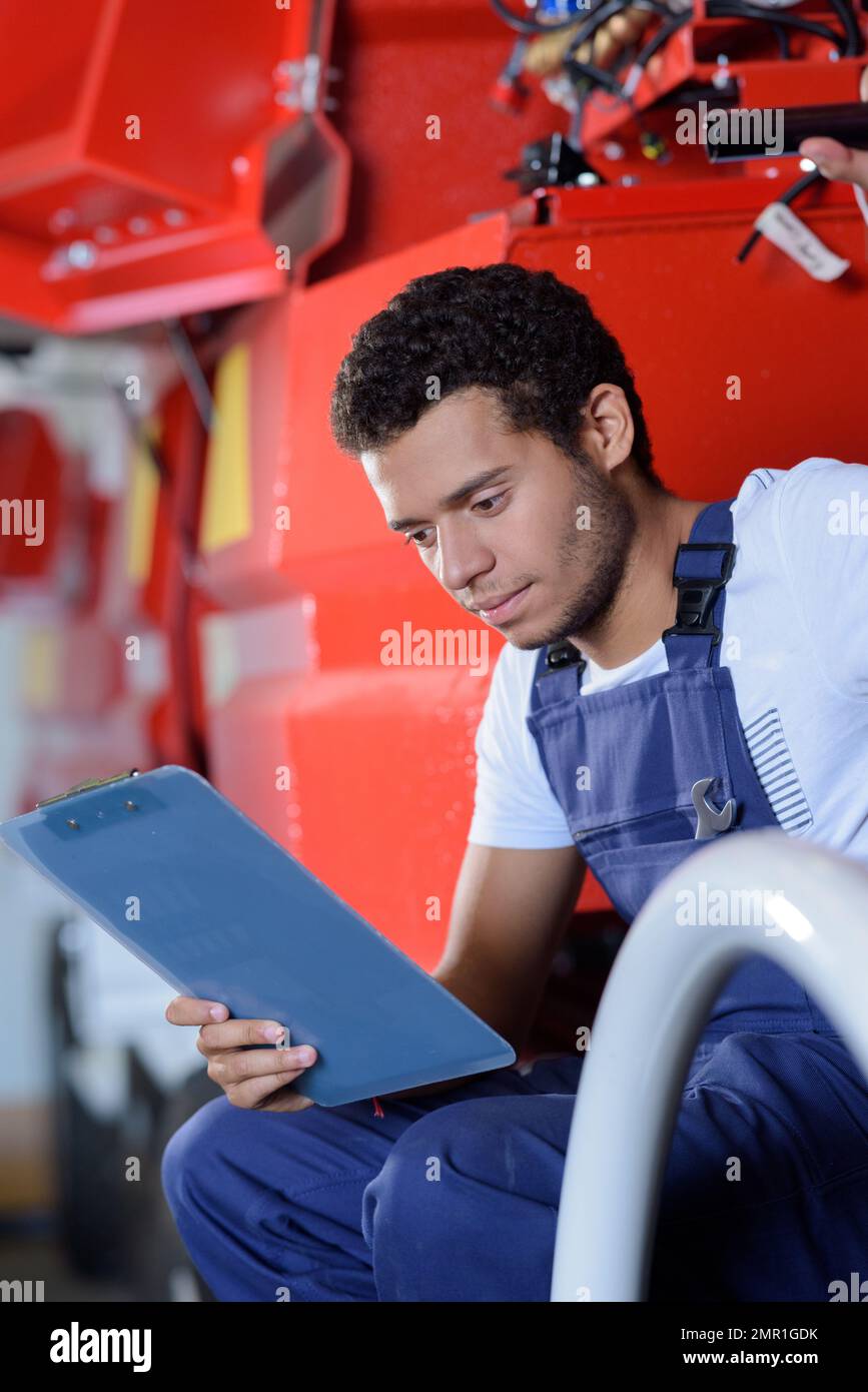 young male mechanic sat on vehicle step reading clipboard Stock Photo ...