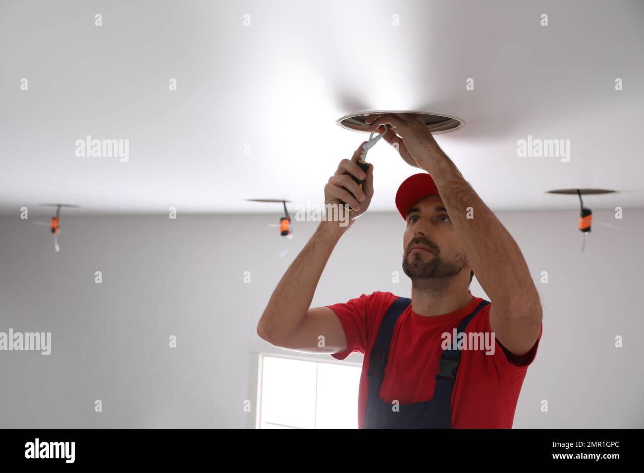Worker installing lamp on stretch ceiling indoors Stock Photo - Alamy