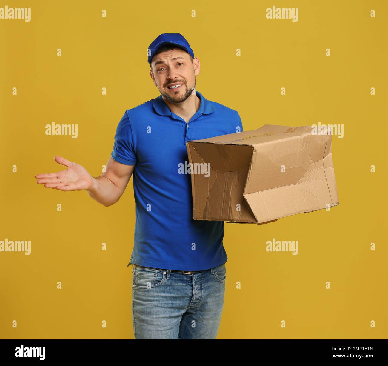 Emotional courier with damaged cardboard box on yellow background. Poor ...