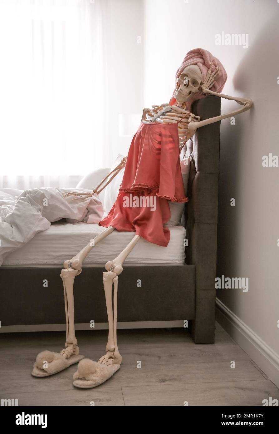 Human skeleton in silk pajamas and towel sitting on bed indoors Stock ...